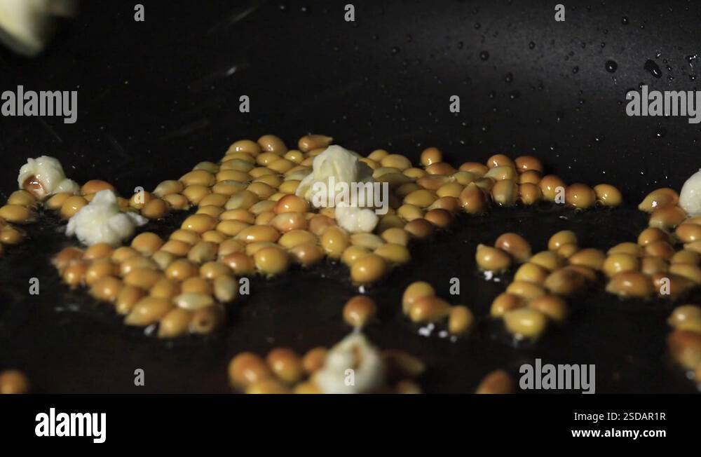 Close up: gold popcorn kernels popping corn in oil in black skillet ...