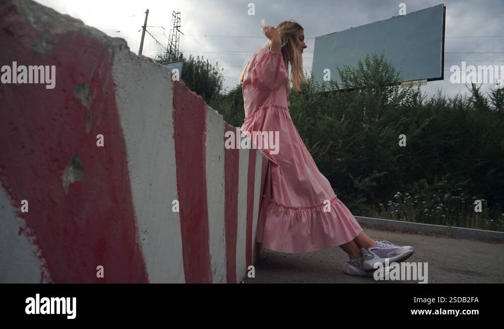 Girl in a pink dress sits on a concrete block, an empty billboard on ...
