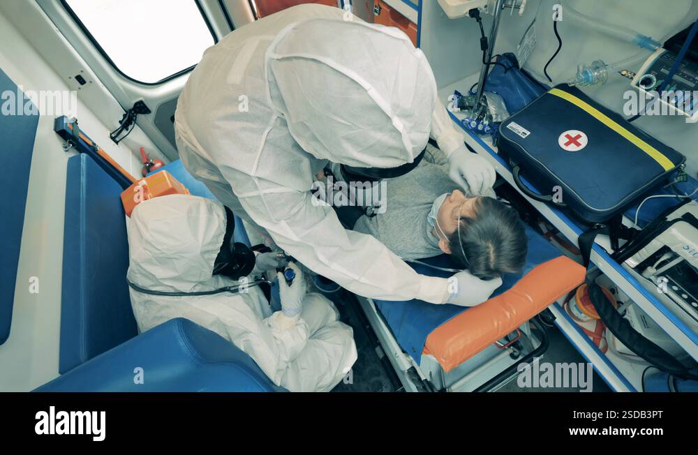 Emergency workers help a man in ambulance car, giving him a ventilator ...