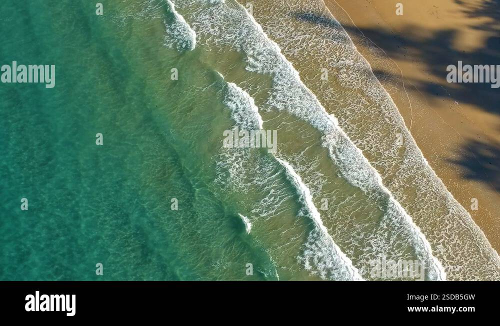 Overhead of small clear waves breaking on tropical beach with tan sand ...