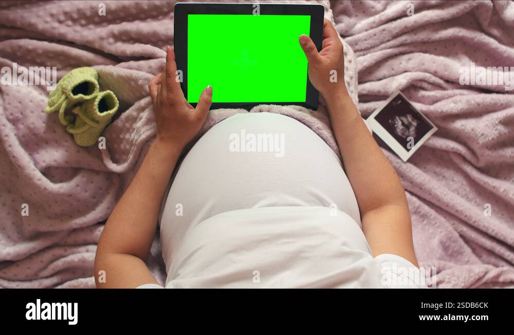 Top view of a pregnant woman lying in bed with a tablet with a green ...
