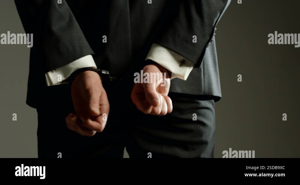 Business man in handcuffs behind back - close up on hands behind back ...