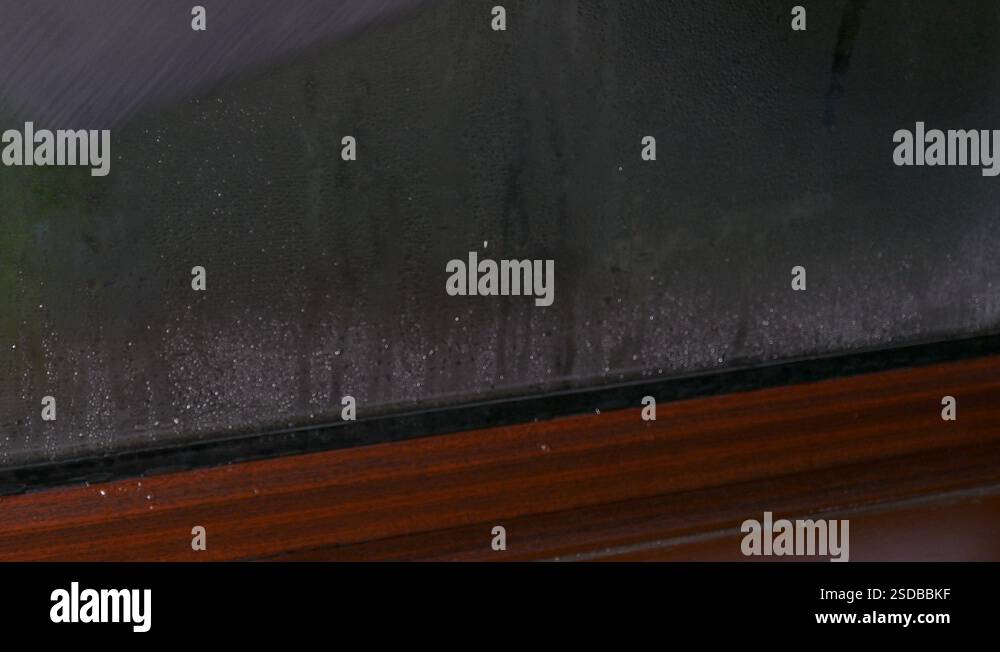 Hand wiping heavy condensation from a glass window with a cloth Stock ...