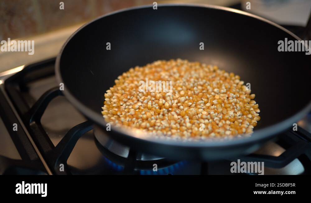 A lot of small yellow seeds frying in cooking pan, preparing of popcorn ...
