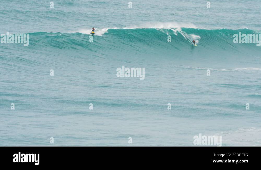 surfer in life jacket rolls on wave in Portugal, instructor and drone ...