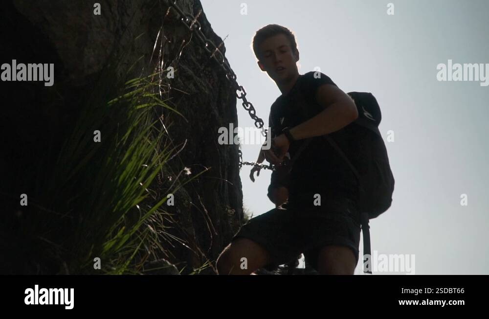 Two young men climbing down rocks while holding a chain, slow motion ...