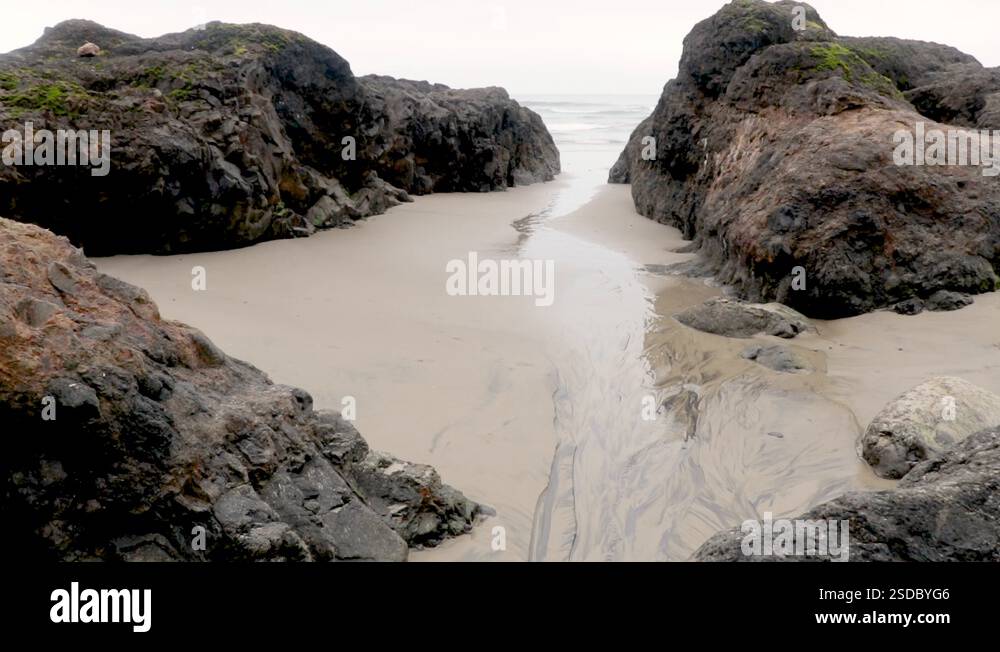 Black sand flowing in small beach stream going to the ocean between two ...
