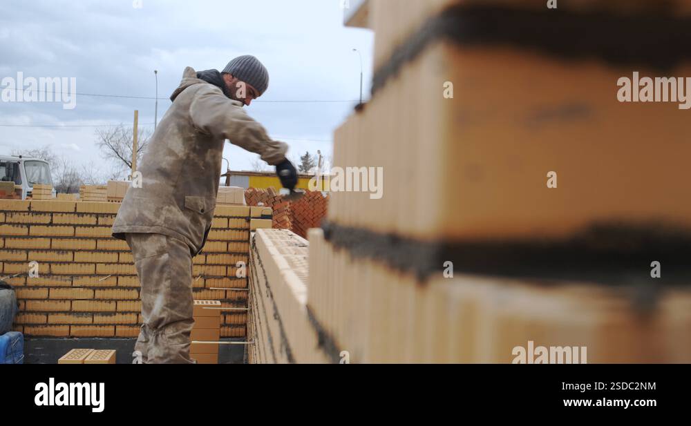 Male builder works at construction site as bricklayer, builds wall of ...