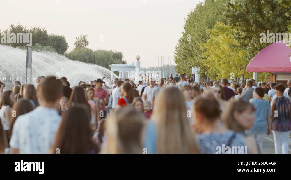 Crowded city park promenade with the fountains on warm summer evening ...