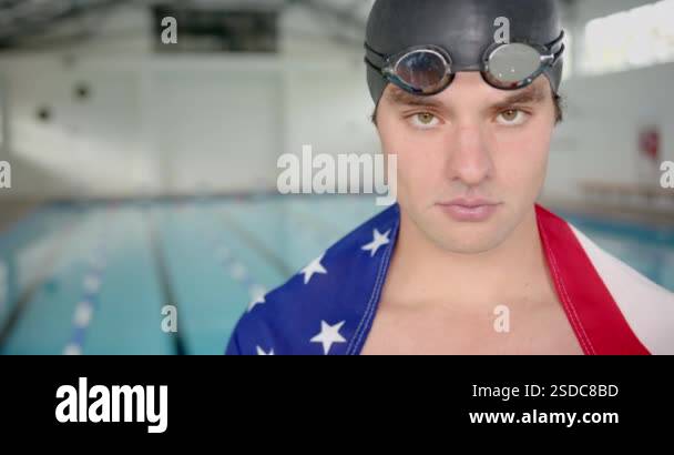 Male Swimmer wearing goggles and flag towel standing by indoor pool ...