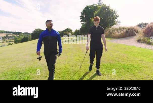 Two male golf players playing golf together, walking with clubs on a ...