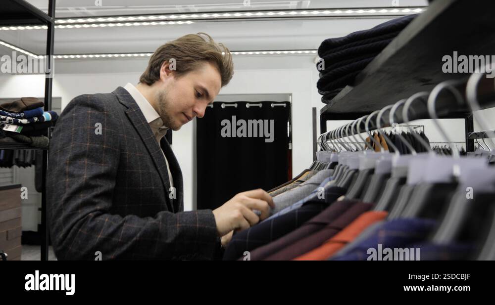Young man guy is shopping choosing classic suit in clothing store, side ...