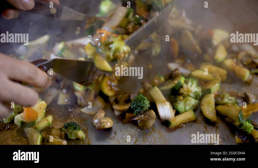 Mixing healthy fresh produce on hot grill in kitchen of Asian ...