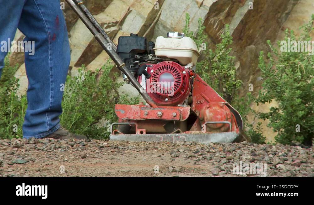 A construction worker walks behind a plate compactor leveling the ...