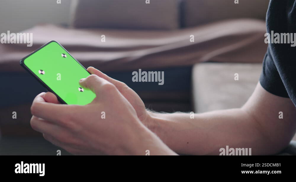 Closeup young man sit on a couch and watch something on a smartphone ...