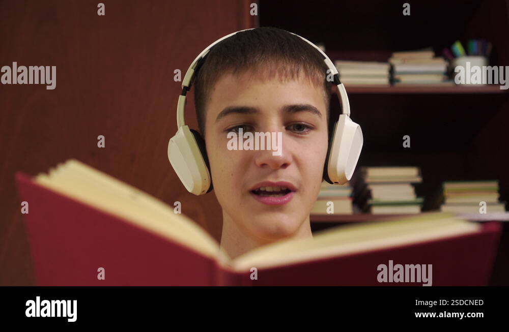 Young student reads out loud a book in headphones against the ...