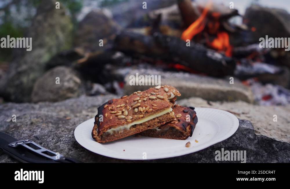 Fried bread with seeds and cheese lies on a stone near a campfire ...