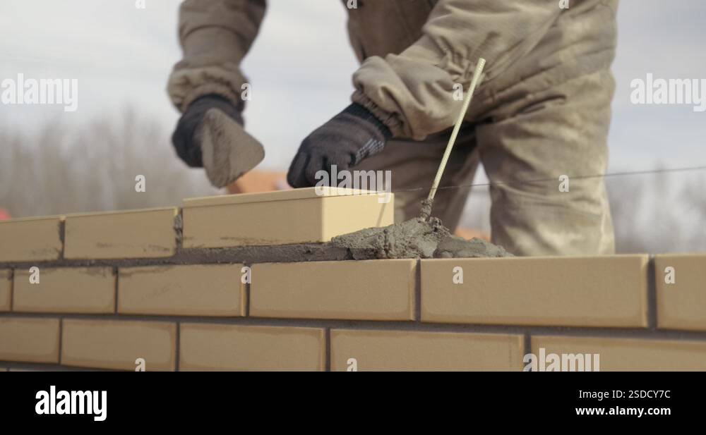 Bricklayer works at construction site, lays bricks in masonry, builds ...