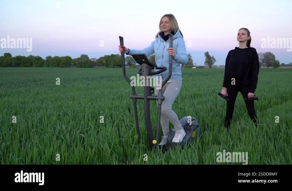 Two young women doing fitness exercises in a green field. Dolly shot ...