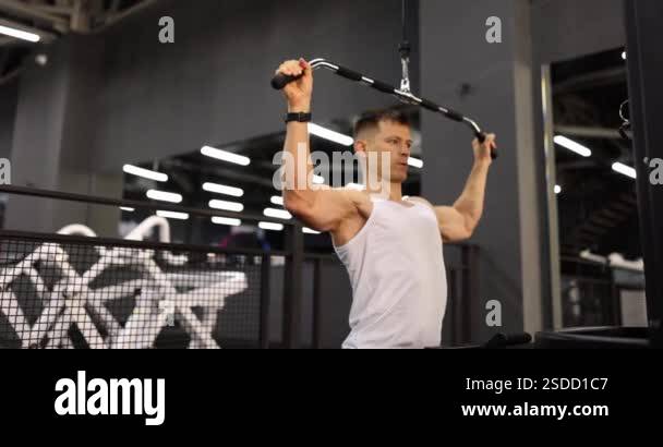 Muscular athlete performs LAT pull-down exercise in gym. Man builds ...