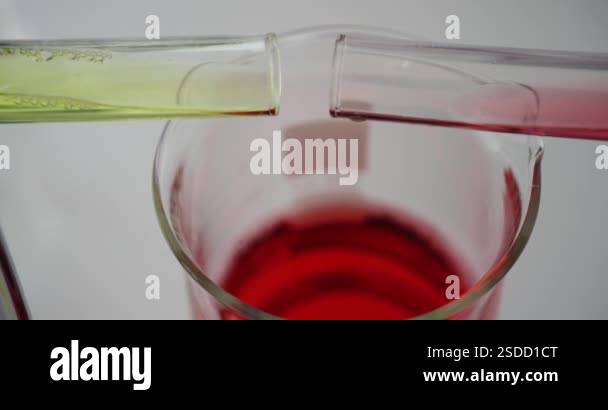 Chemical liquids stream from test tubes into beaker in lab. Generating ...