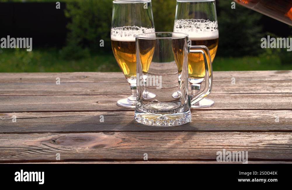 Fresh beer is pouring into glasses, outdoors on blurred background ...