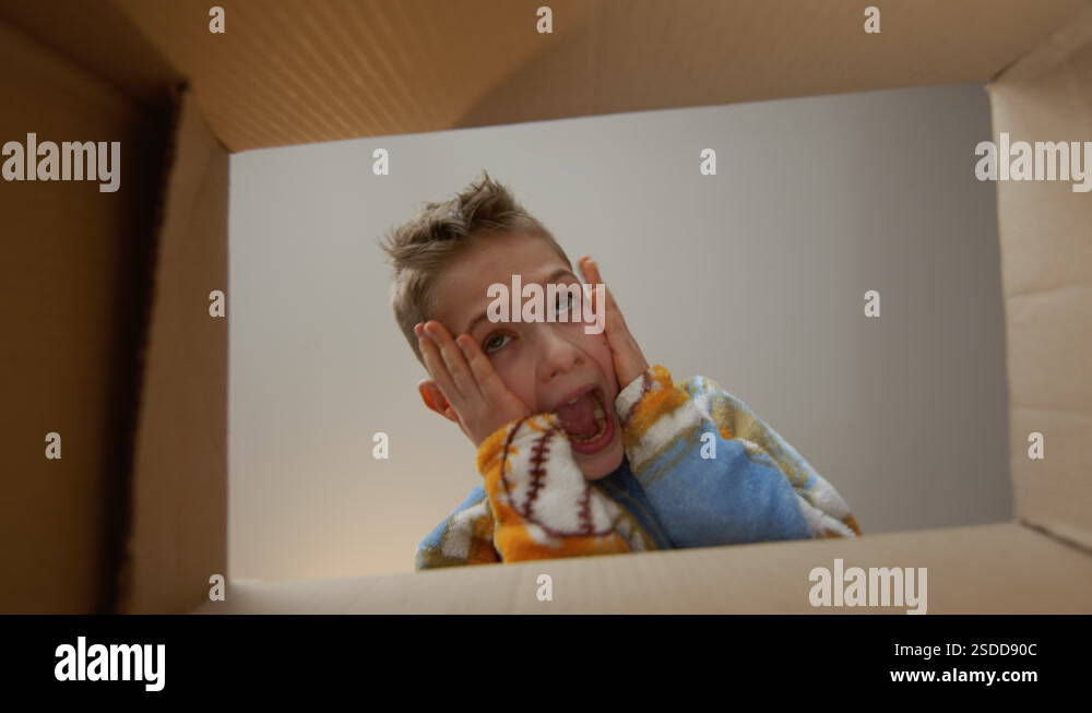 Boy Opens Cardboard Box. Little Boy Shows Funny Grimaces Looking In ...