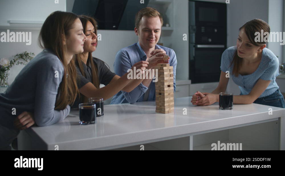 Friends are sitting in the kitchen and playing a board game of jenga ...