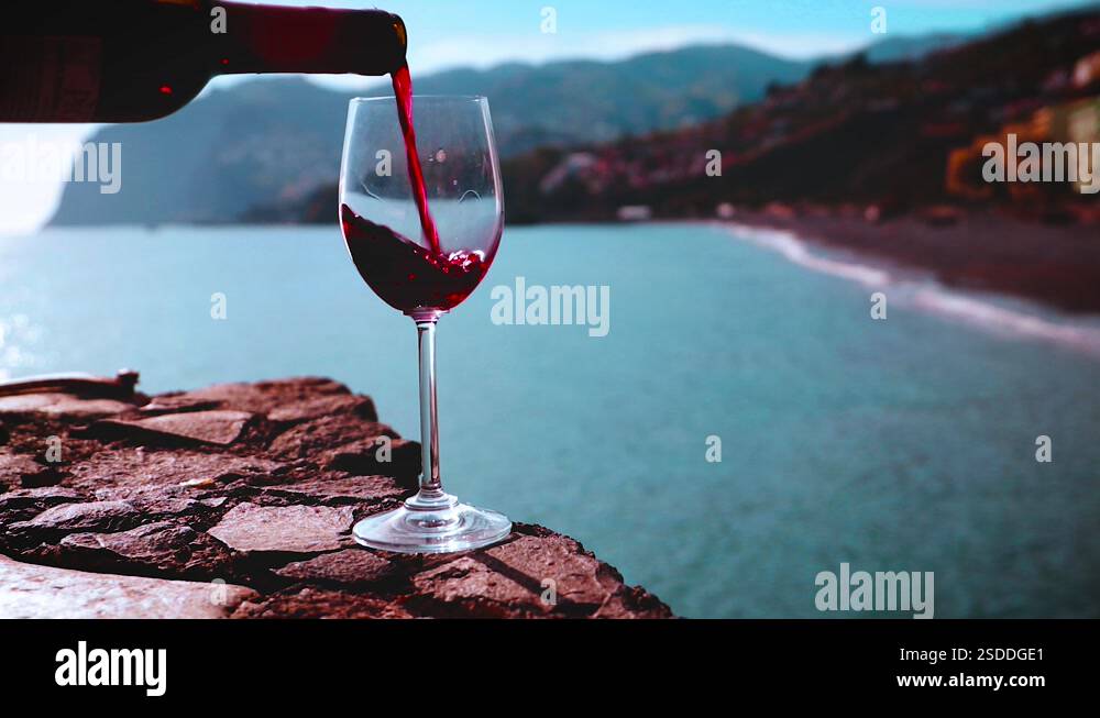 Red wine poured into wine glass overlooking beach with mountains ...