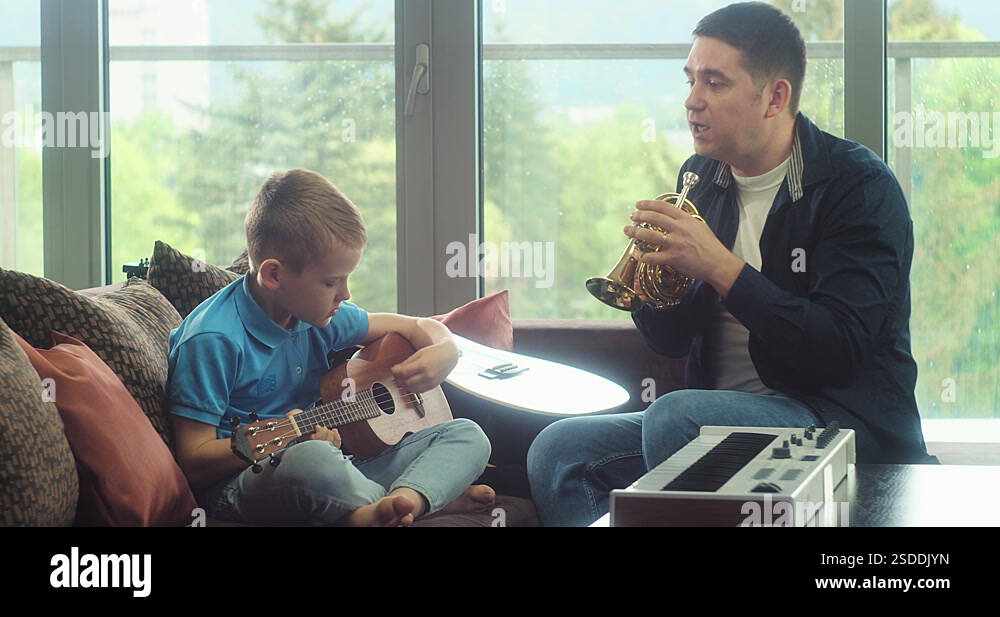 Father and son play guitar and trumpet at home. Dad teaches child to ...
