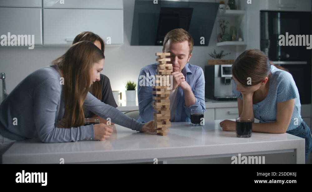 Friends are sitting in the kitchen and playing a board game of jenga ...