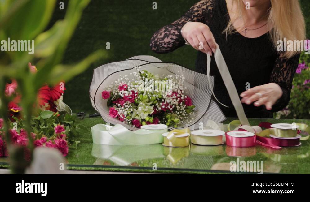 Professional woman florist unwinds the red ribbon, cuts it with ...
