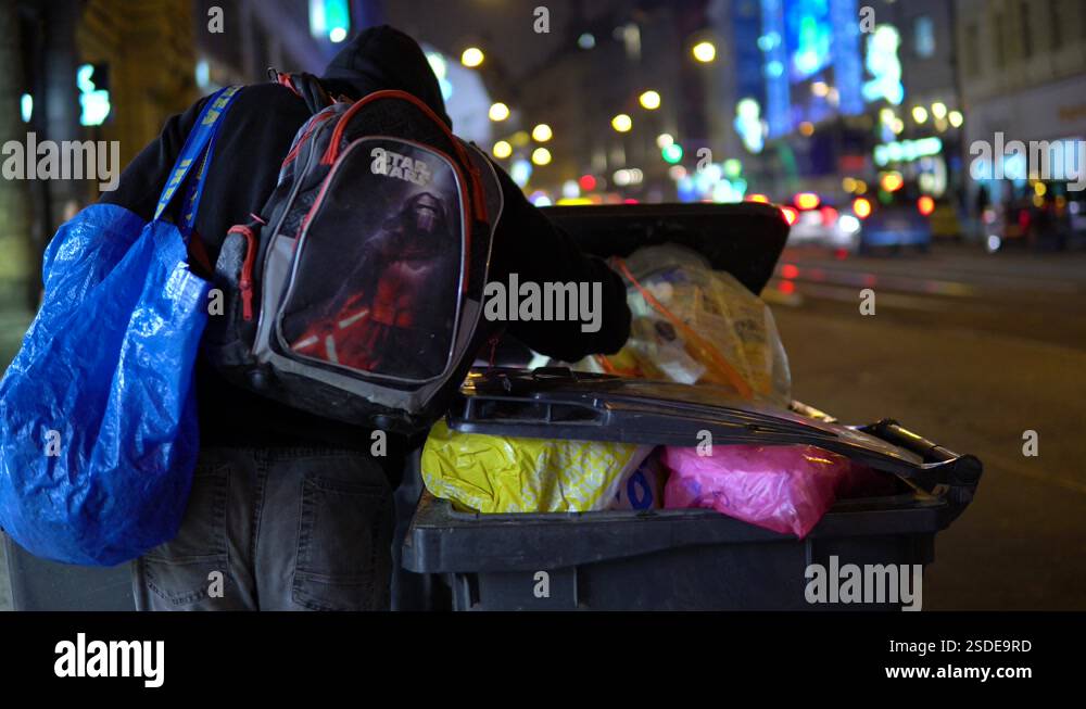 A homeless man looks through crowded garbage bins on the street at ...