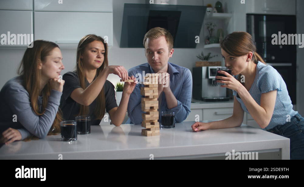 Friends are sitting in the kitchen and playing a board game of jenga ...