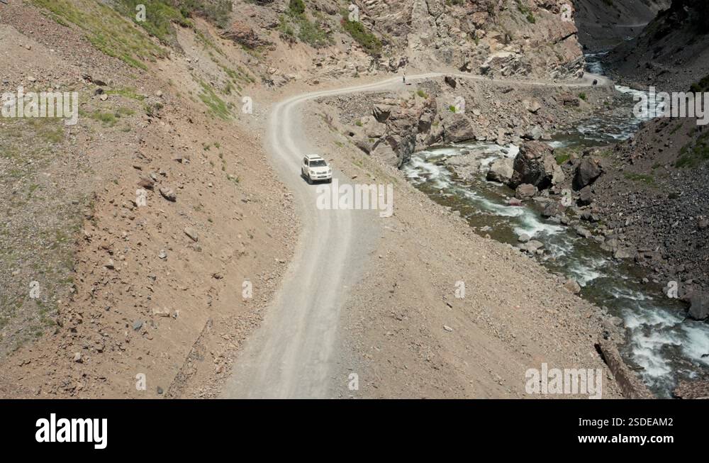 White SUV driving on a dangerous cliff road, hillside of a barren ...