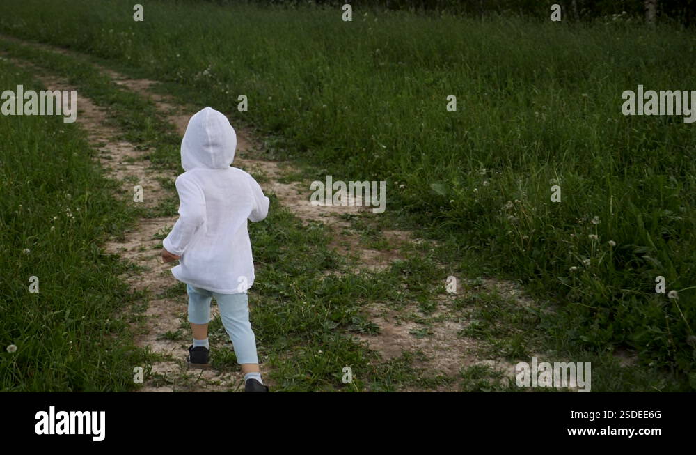 boy in blue pants and a white jacket in a hood runs along the road ...