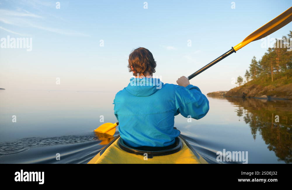 outdoor activities, man in slowly rowing oars in kayak on calm lake ...