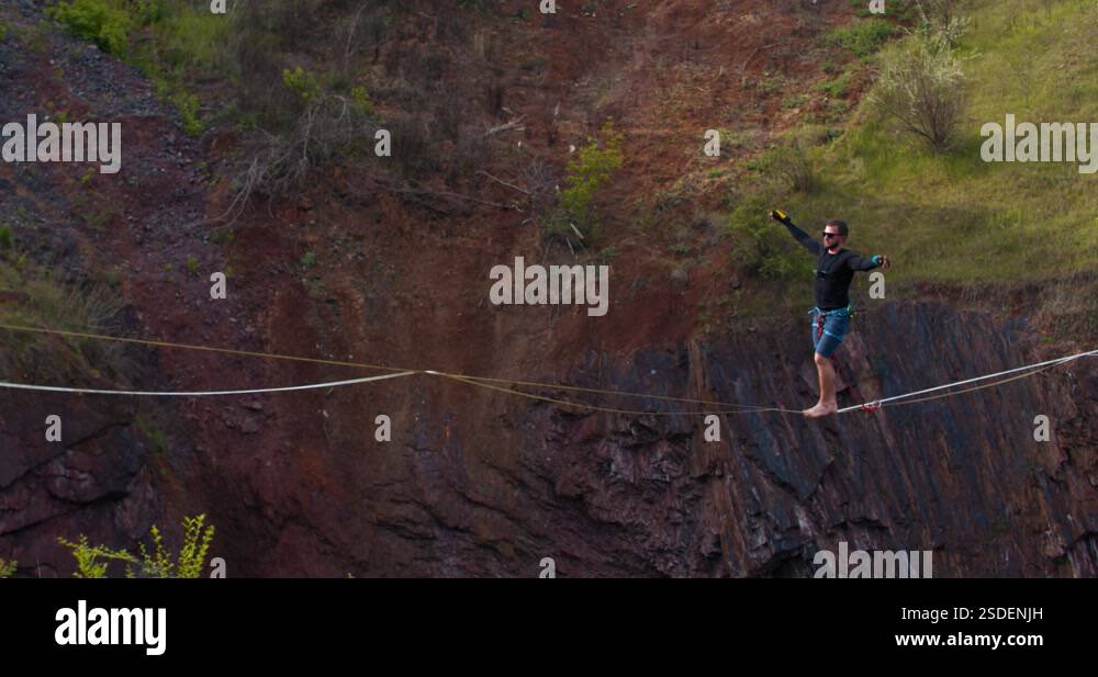 Slackliner is walking on the tightrope over a quarry, sitting down, 4k ...