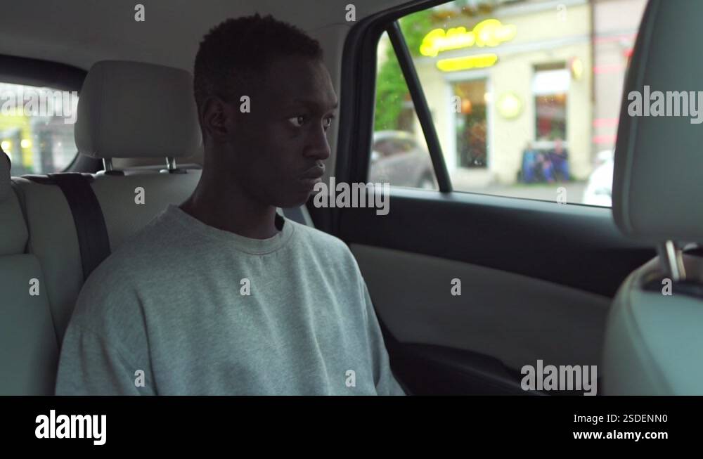 Handsome young black man rides on back seat of a car, looks around in ...