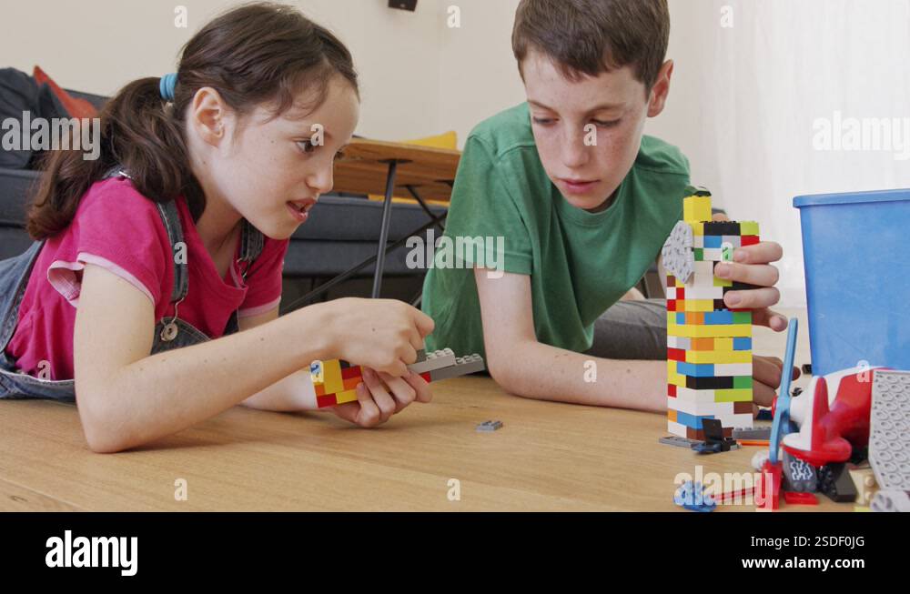 Girl and a boy playing and constructing with toy bricks on the living ...