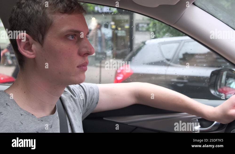 A young blond man bored in a traffic jam sitting behind the wheel of ...