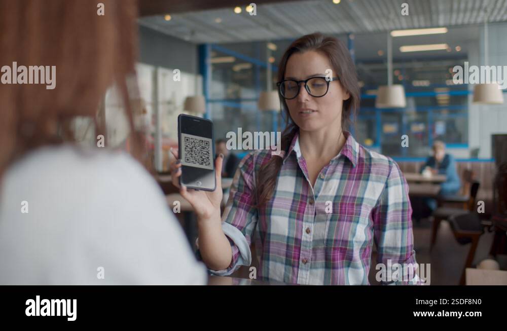 Barista scanning QR code in customer smartphone at counter in cafeteria ...