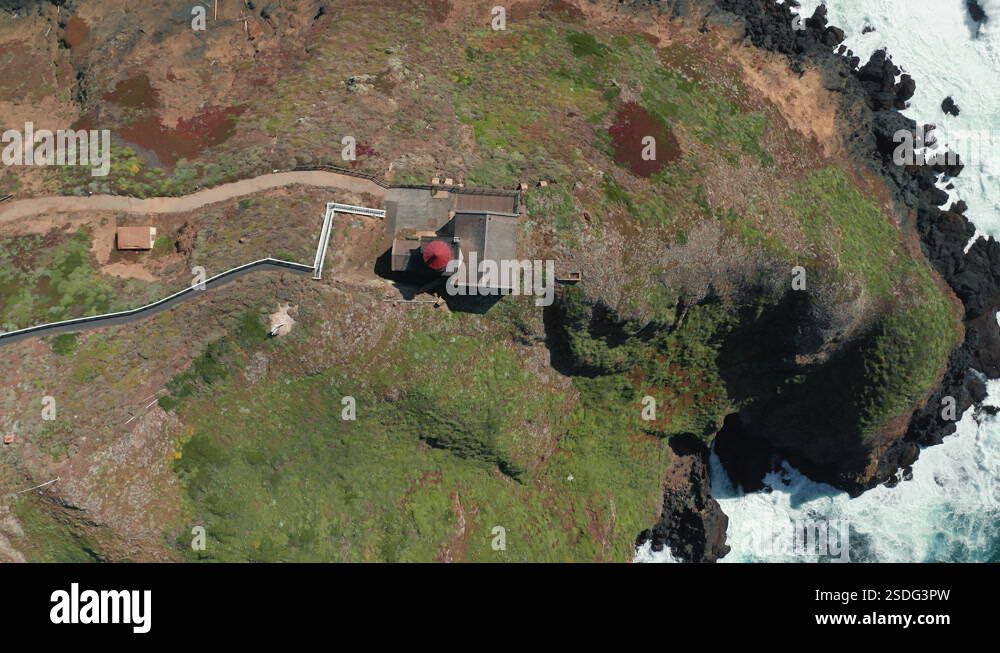 Cinematic overhead view on a lighthouse with red roof on green rocky ...