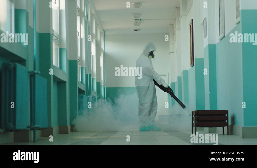This video shows a man in protective overalls sanitizing a school ...