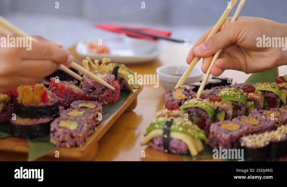 Sushi dinner. Side view of two hands picking up sushi rolls with ...