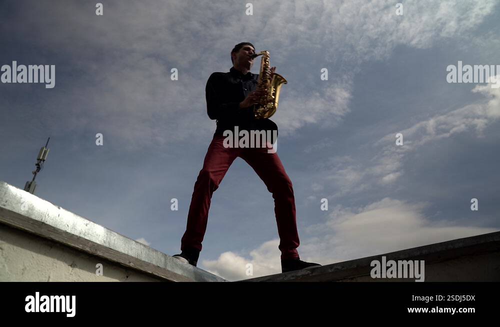 saxophonist is playing music, tilt up view against blue sky with clouds ...
