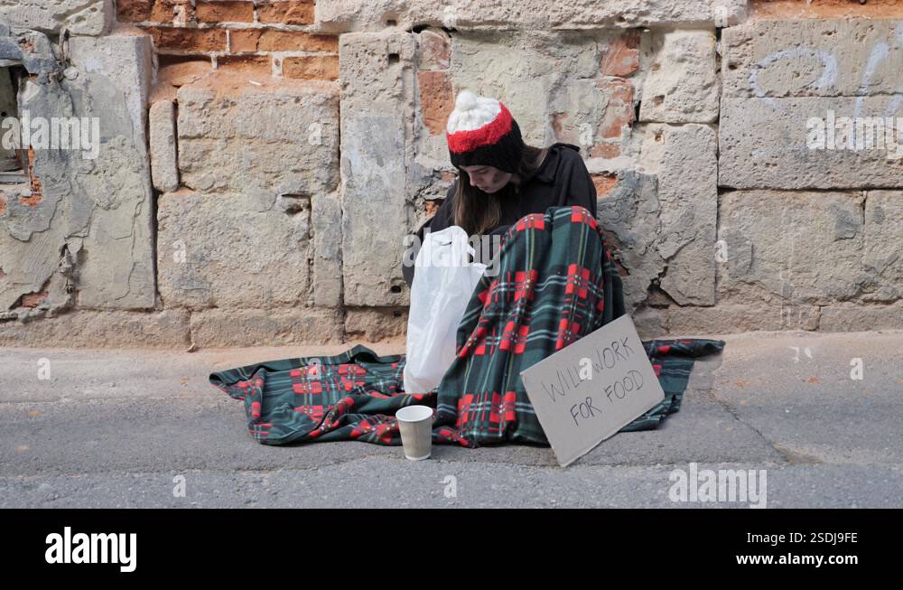 Homeless girl sitting on the street and opens a package of food Stock ...