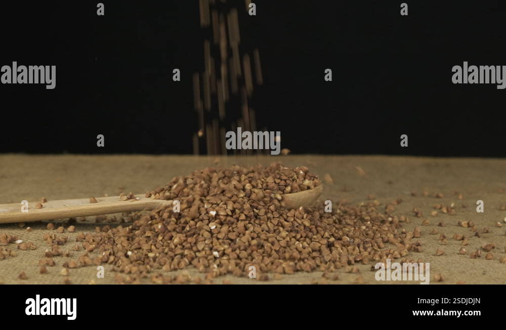 Buckwheat grains fall into a wooden spoon and heap is poured. Slow ...