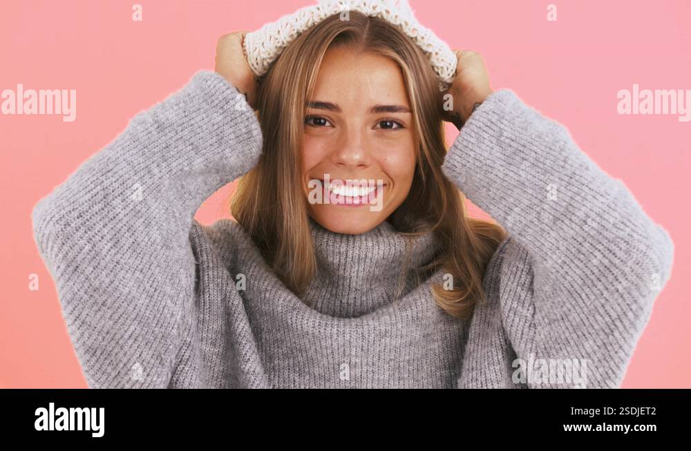 Young lady in warm sweater is putting on white hat and smiling while ...