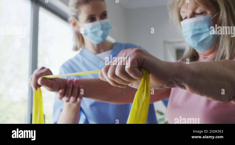 Female health worker assisting senior woman to exercise with exercise ...
